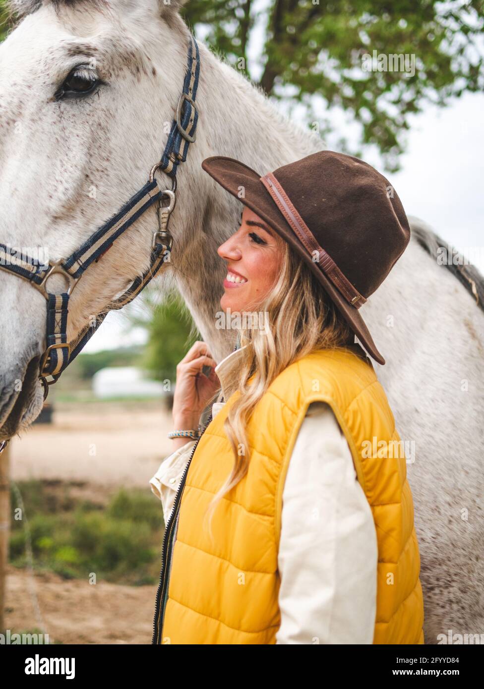 Happy young female equestrian in trendy outfit and hat smiling while ...