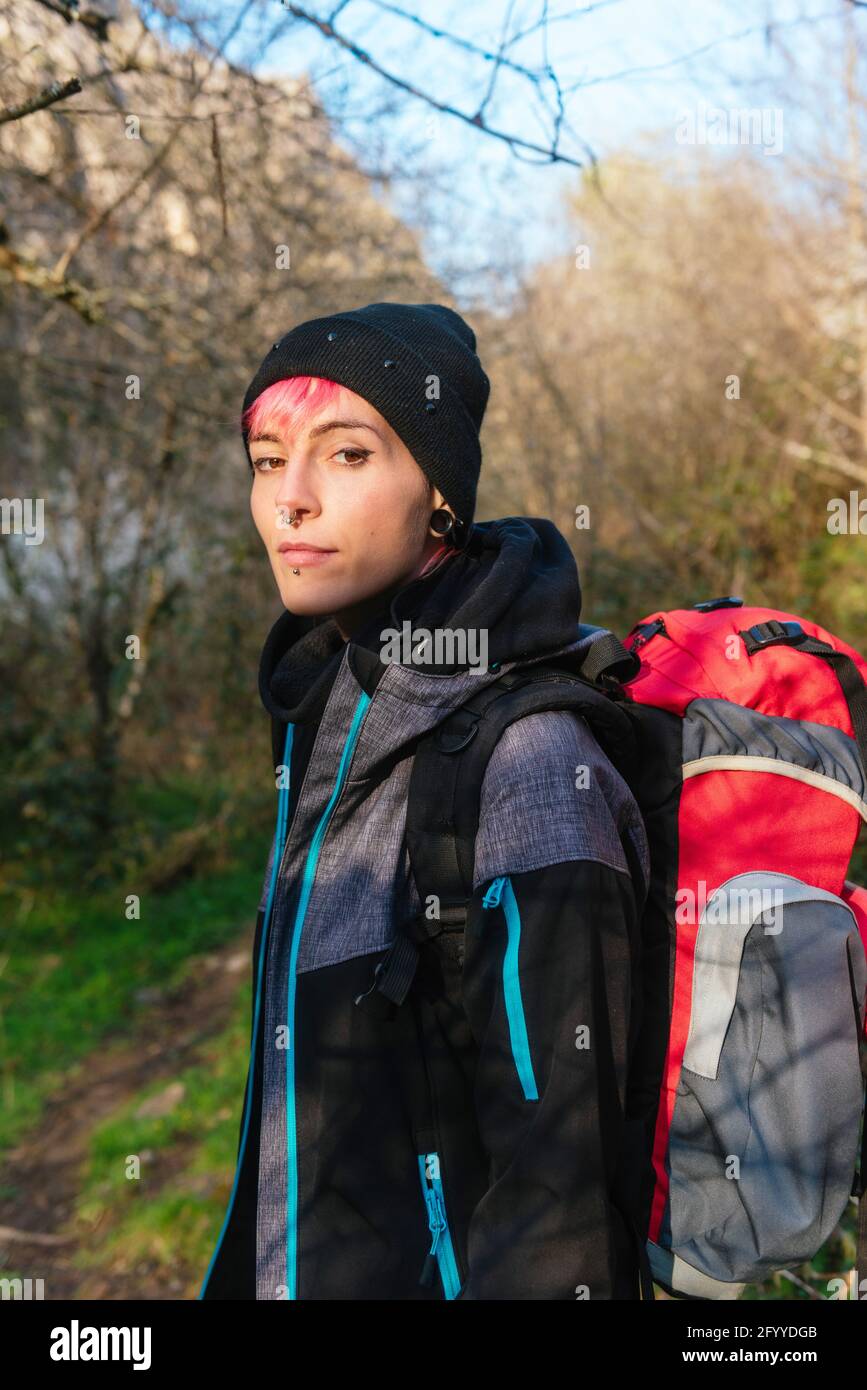 Serious female explorer wearing hat and outerwear with backpack looking ...