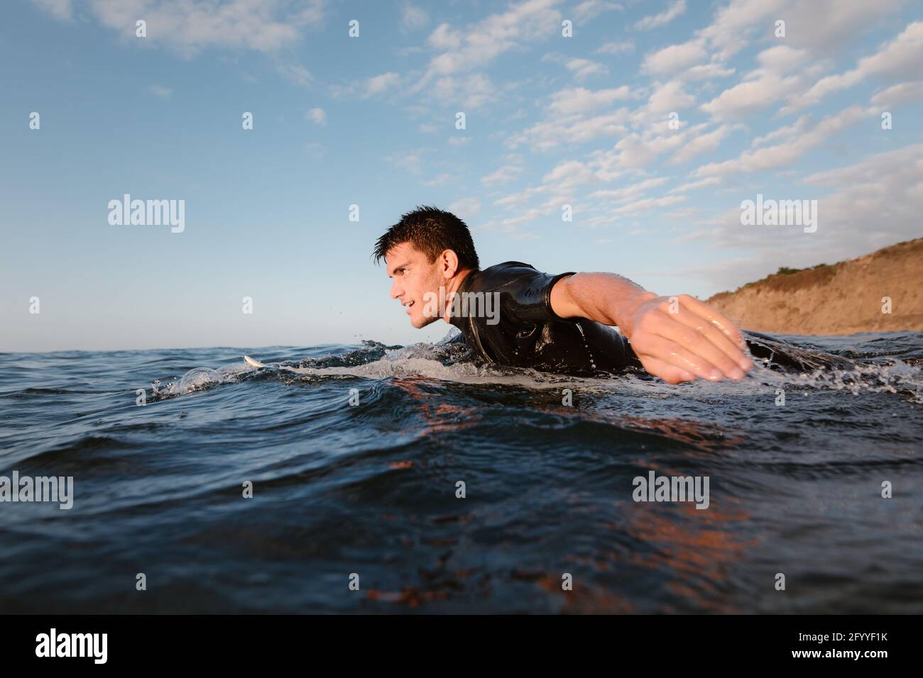 Side view of male athlete in wetsuit swimming in rippled sea while ...