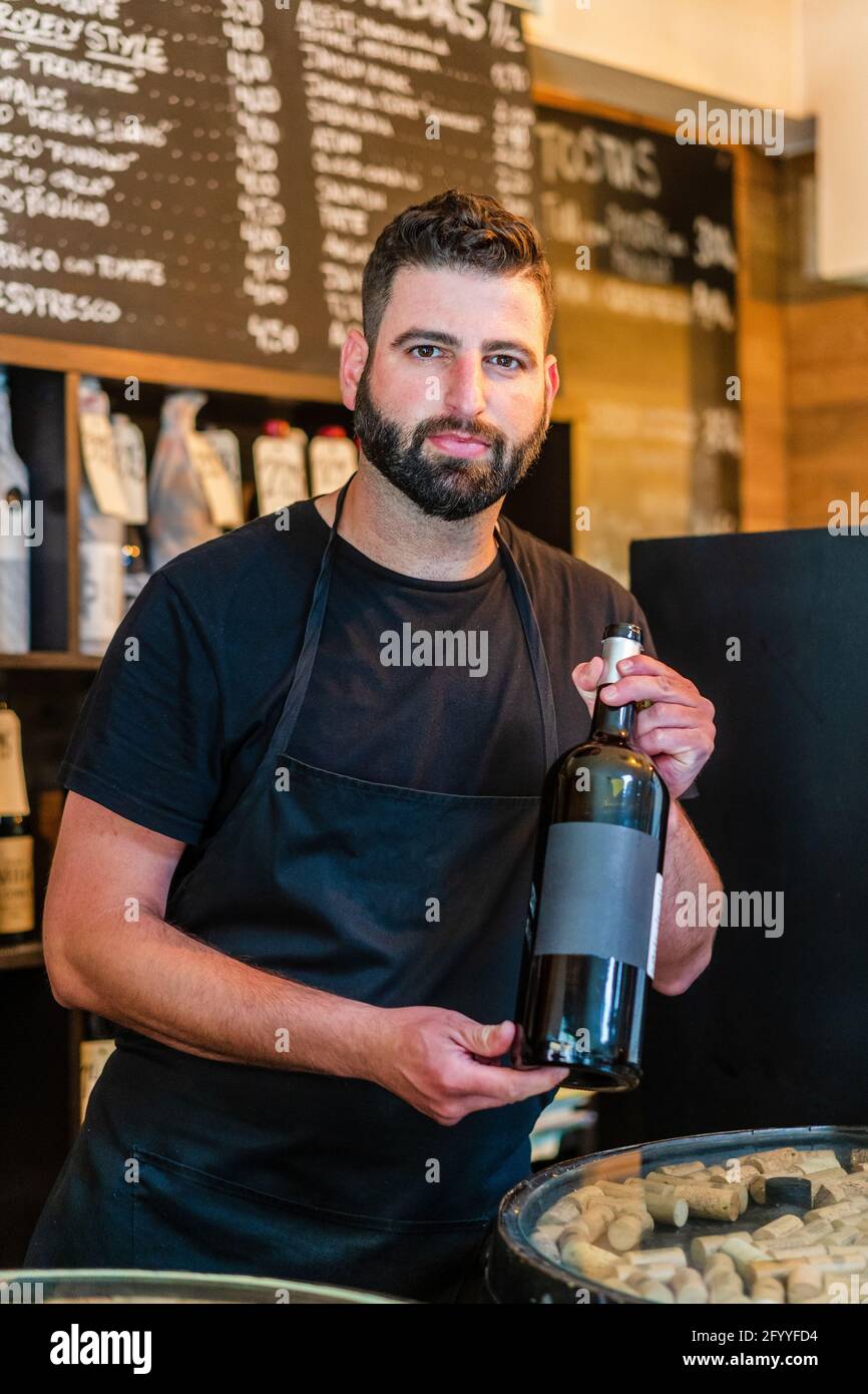 Serious bearded barman with dark hair in black apron standing at ...