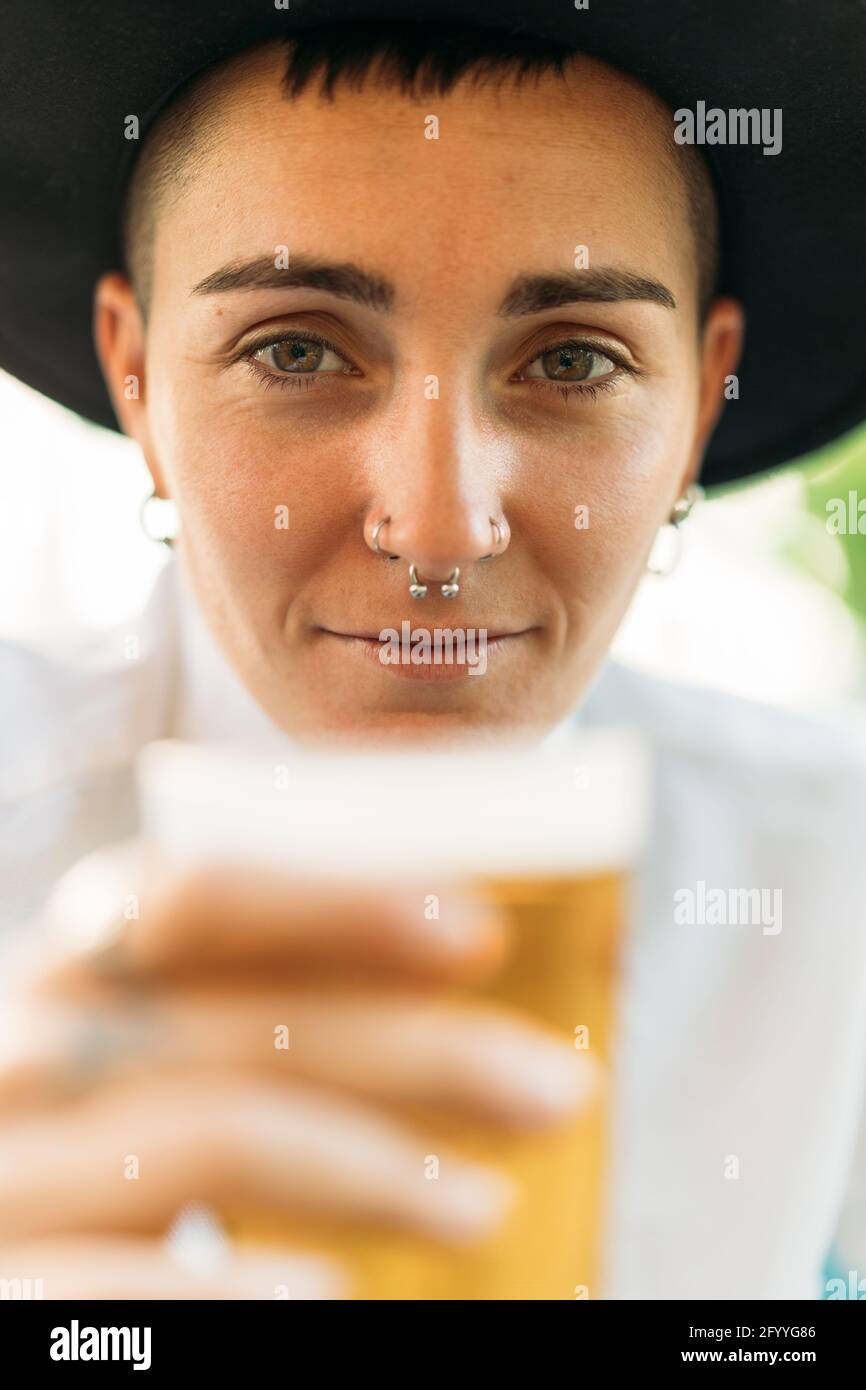 Positive tomboy with tattoos wearing hat and white shirt drinking beer ...