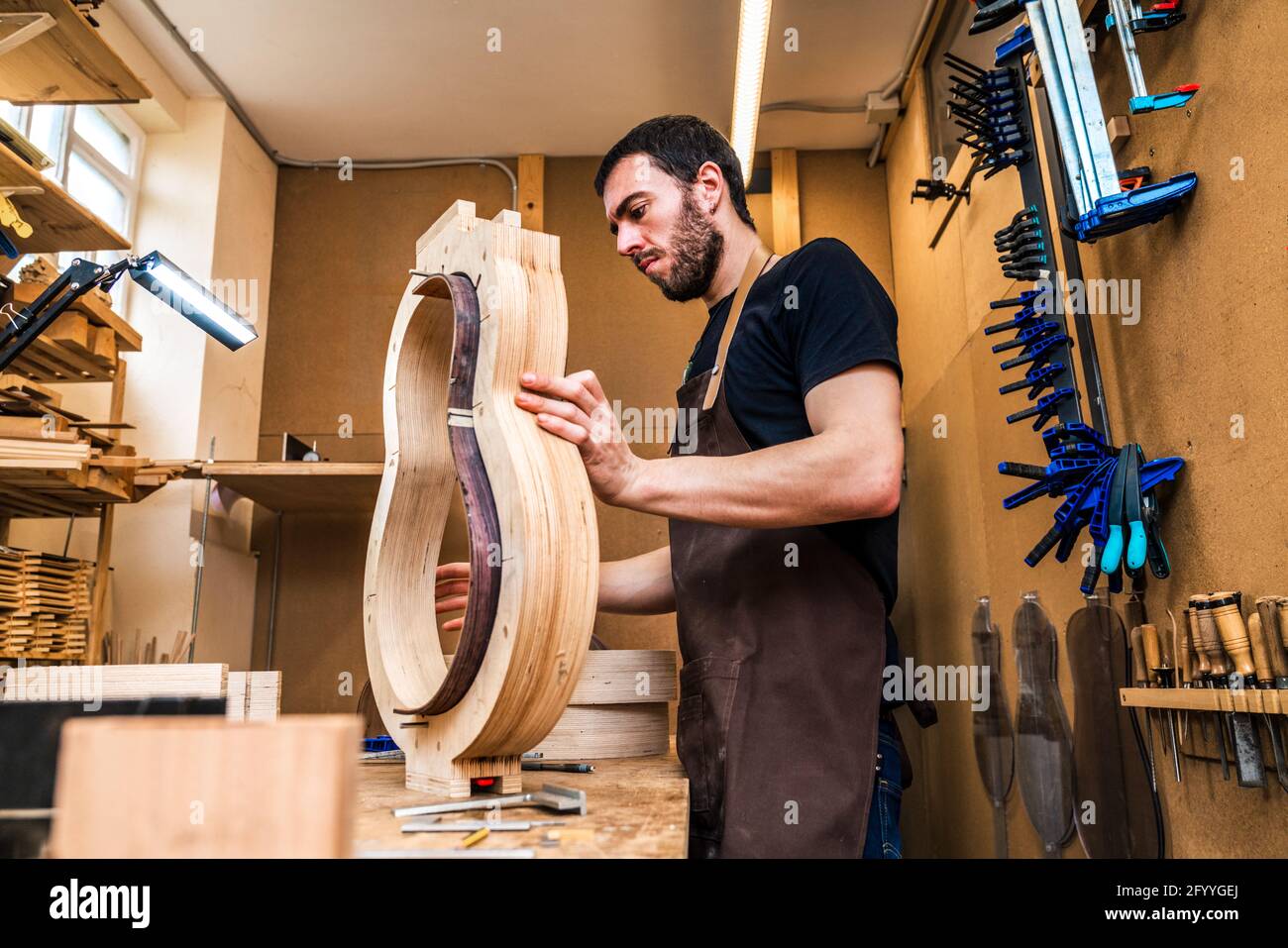 Side view of male luthier making wooden musical instrument at table in ...