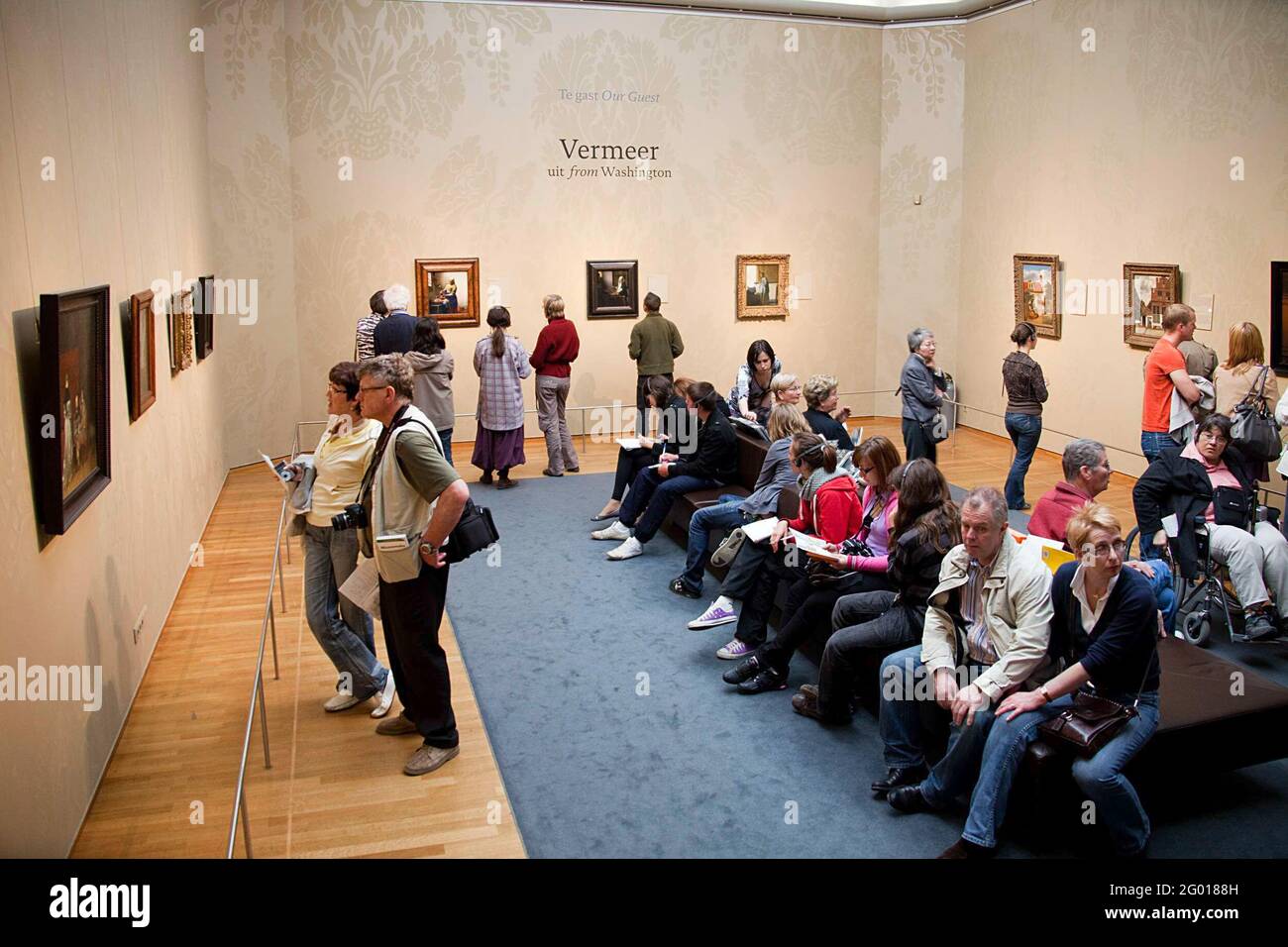 Room with paintings by Vermeer and standing and sitting visitors; Guest ...