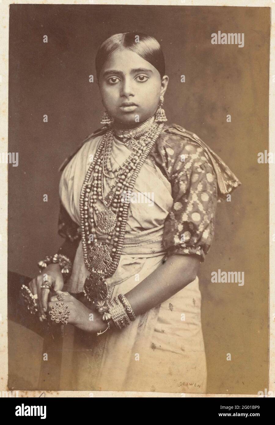 Portrait of a young woman dressed in sari and wallpapered with jewelry ...