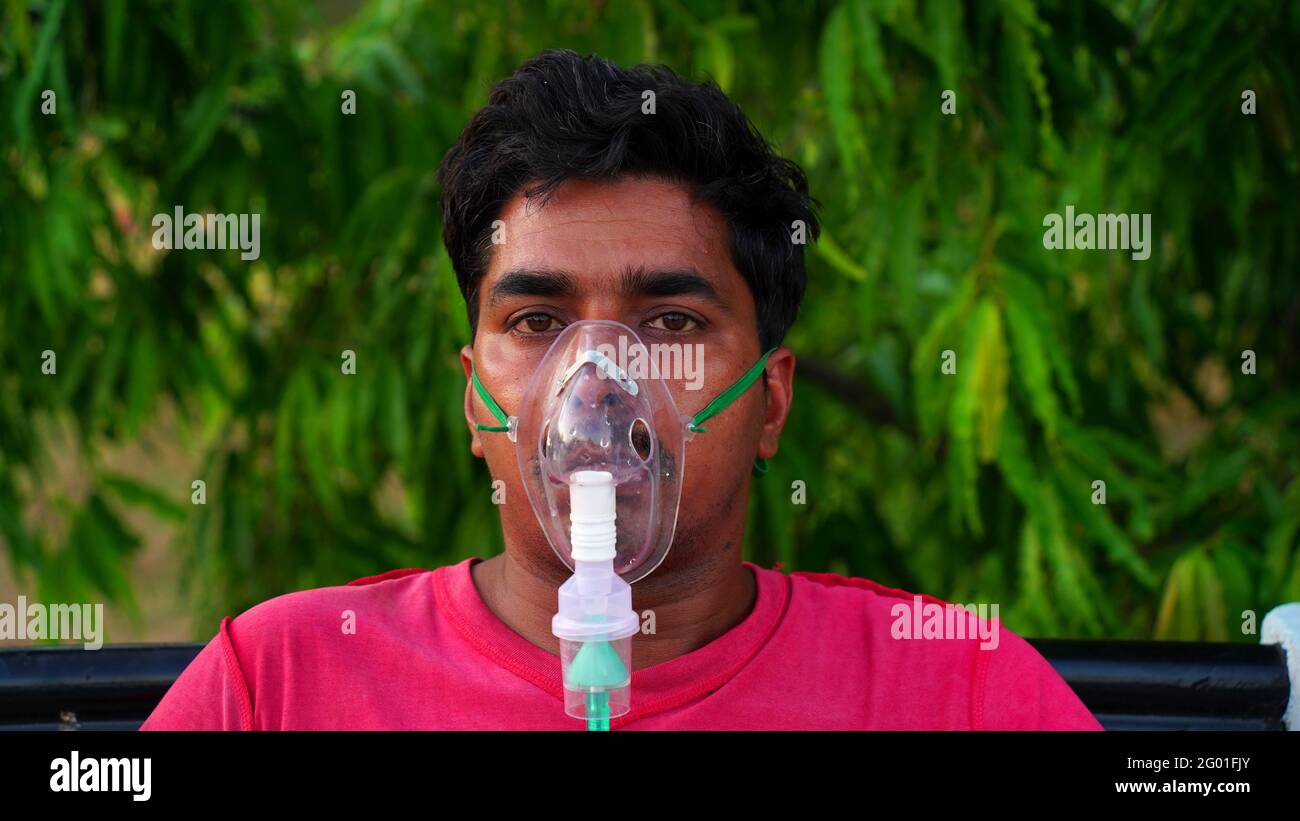 Young man inhale with oxygen mask on face during pandemic in India. A ...