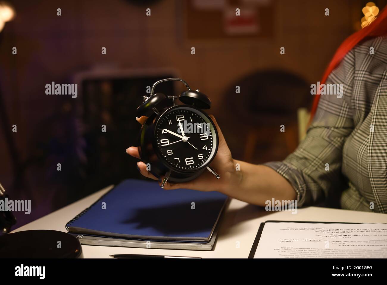 Young woman with alarm clock in office at night Stock Photo - Alamy