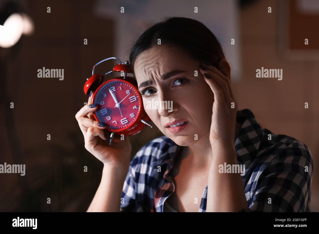 Tired beautiful woman with alarm clock in office at night Stock Photo ...