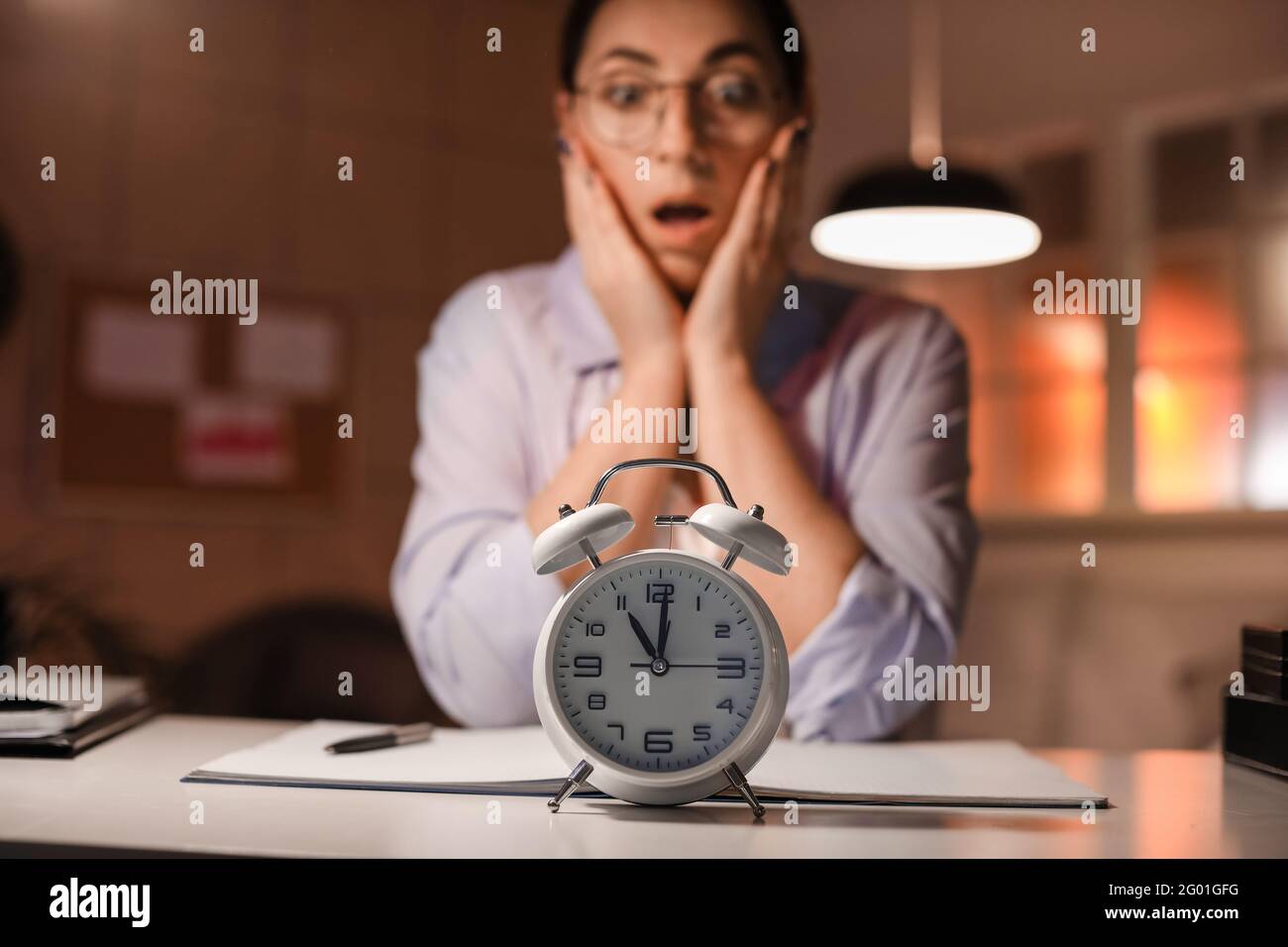 Alarm clock on table of shocked woman in office at night Stock Photo ...