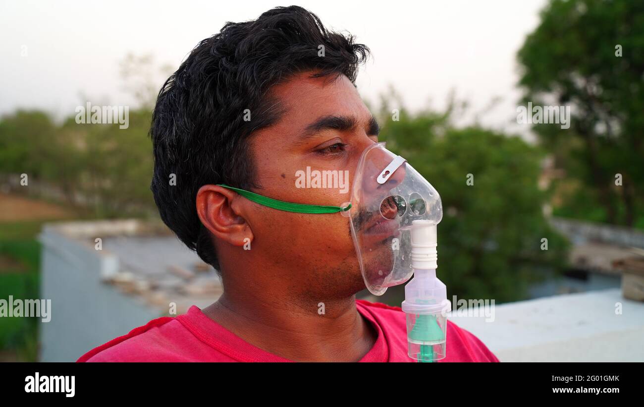 Young man inhale with oxygen mask on face during pandemic in India. A ...
