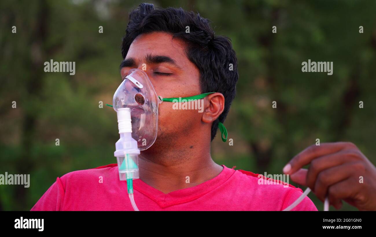Young man inhale with oxygen mask on face during pandemic in India. A ...