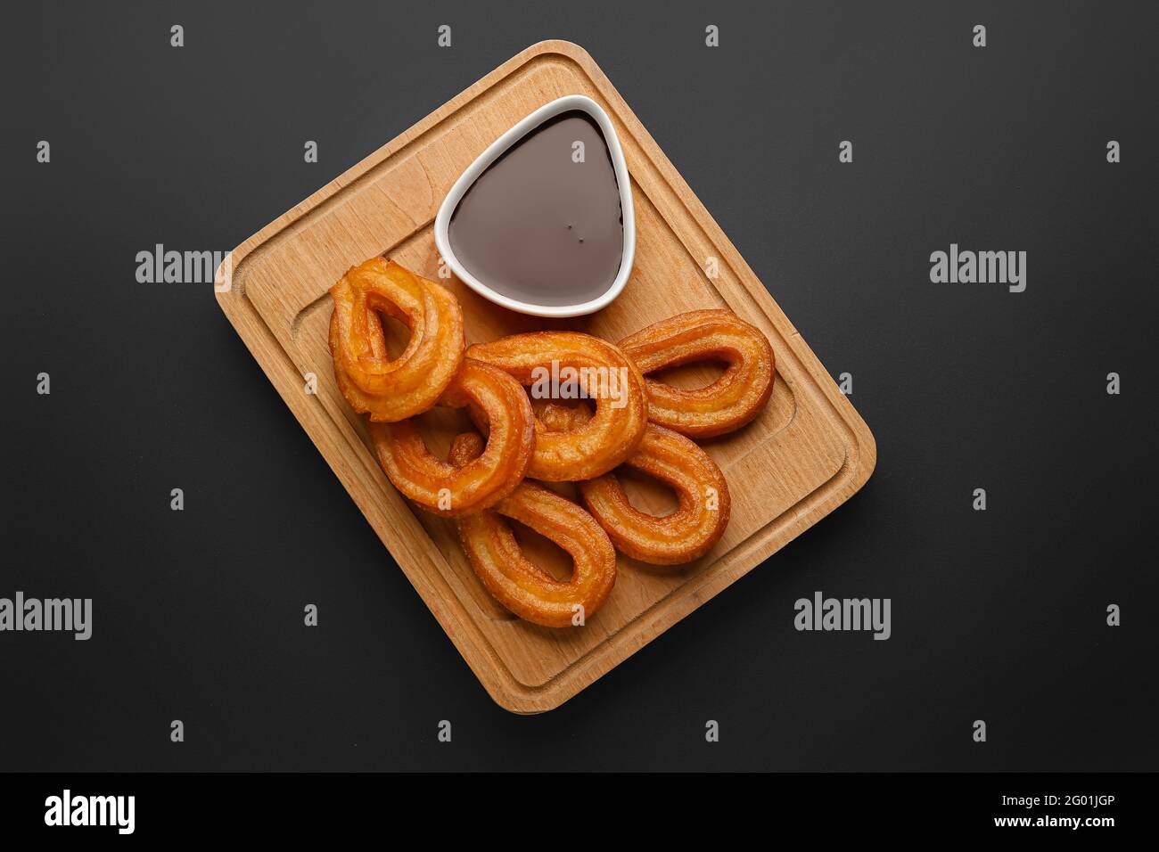 Board with tasty churros and melted chocolate sauce on dark background ...