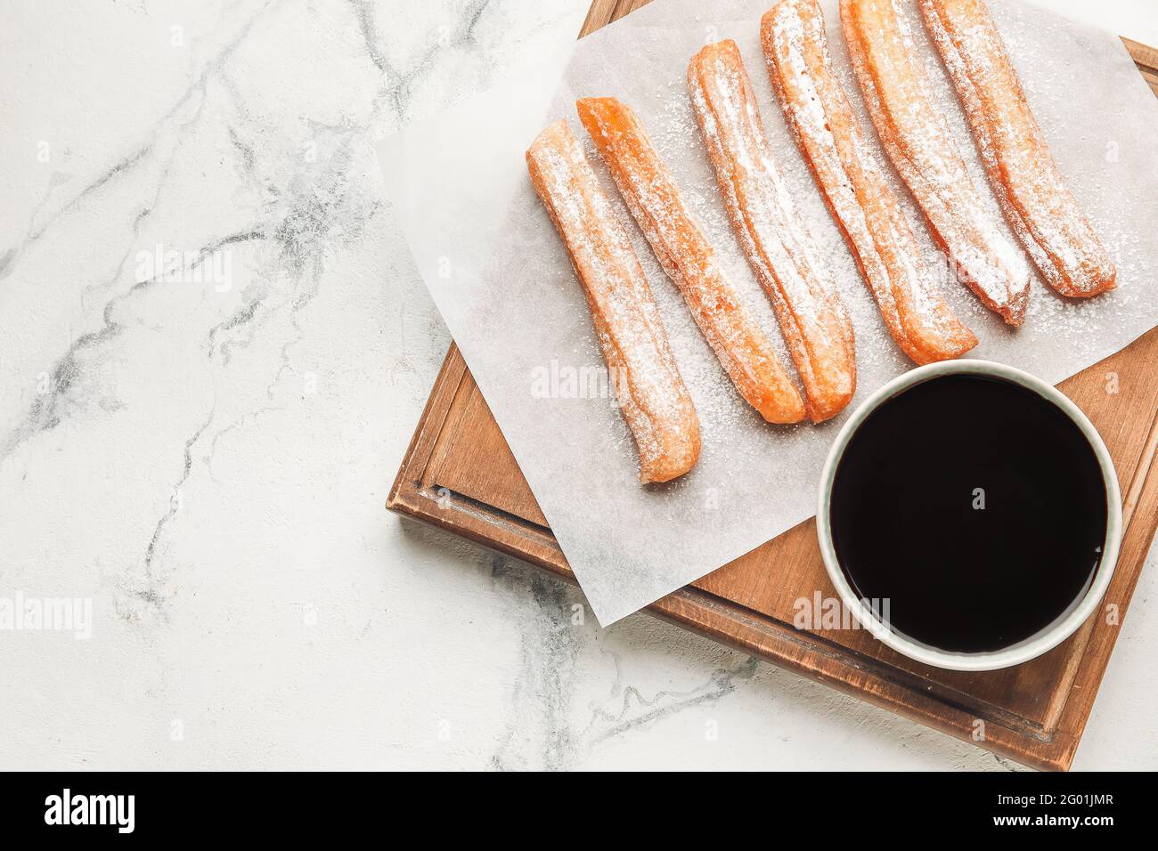 Board with tasty churros and melted chocolate sauce on light background ...