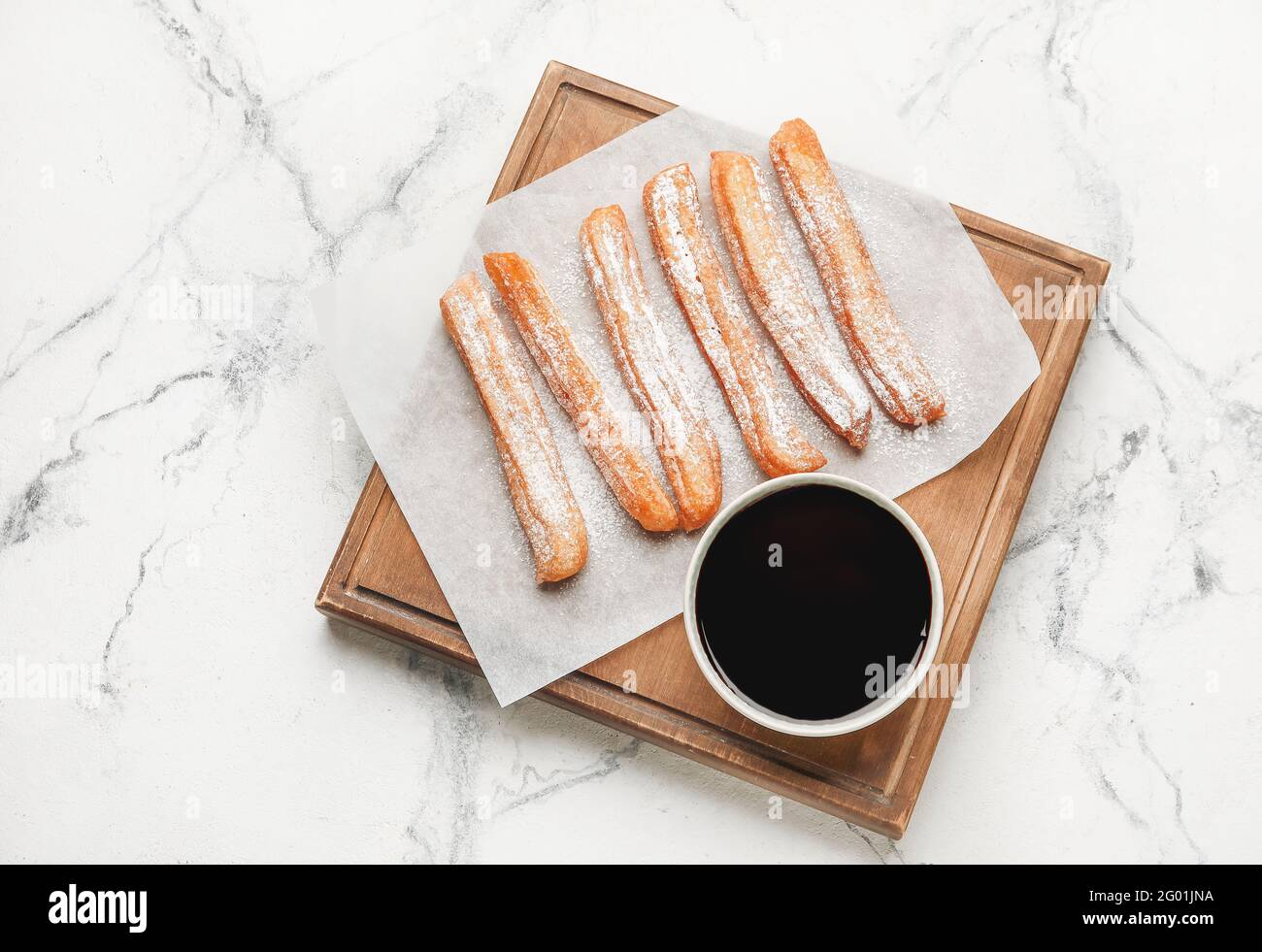 Board with tasty churros and melted chocolate sauce on light background ...