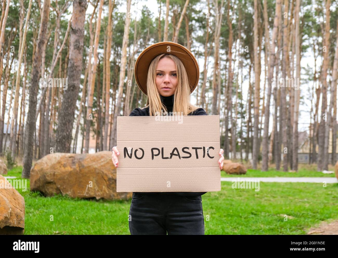 Portrait of caucasian young woman in hat holding cardboard with text NO ...