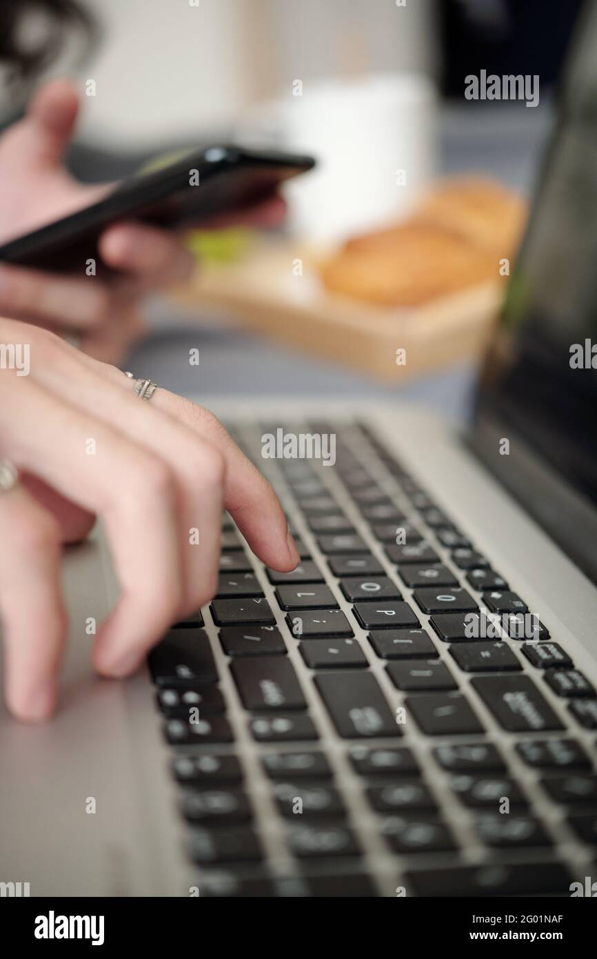 Close-up of unrecognizable man using smartphone while typing on laptop ...
