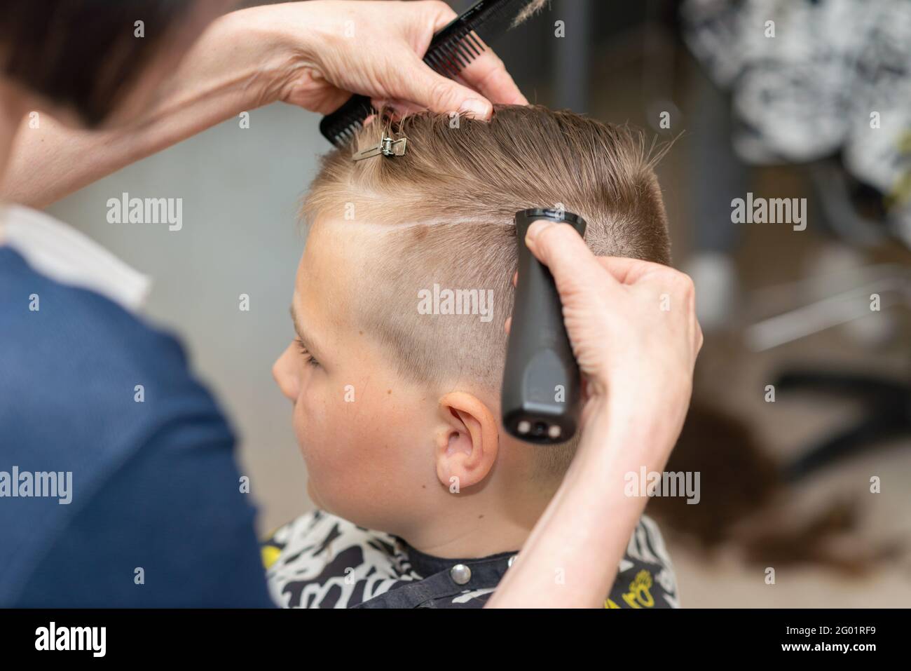 Hairdresser makes a fashionable pretty hairstyle for the young boy in a ...