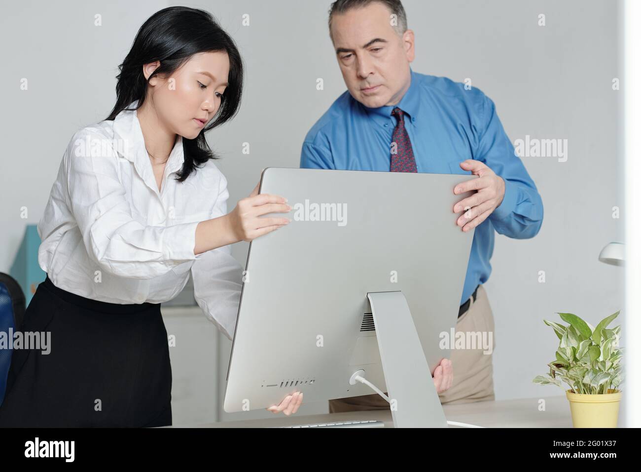 Mature serious man helping new colleague to put computer at her office ...