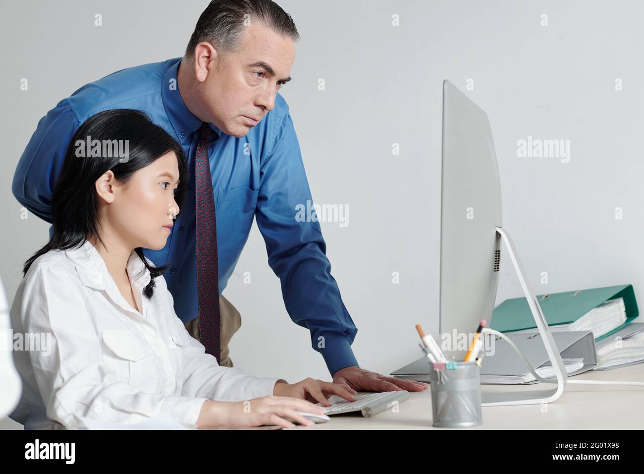 Serious entrepreneur looking at computer screen of employee working on ...
