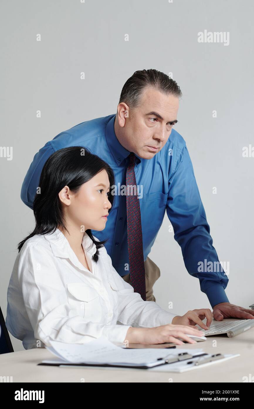 Serious young woman working on computer, her boss is checking if she is ...