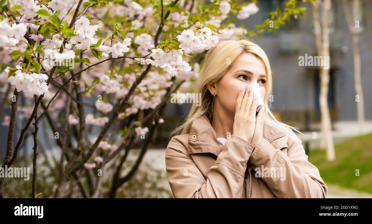 Young pretty girl blowing nose in front of blooming tree. Spring allergy concept Stock Photo - Alamy