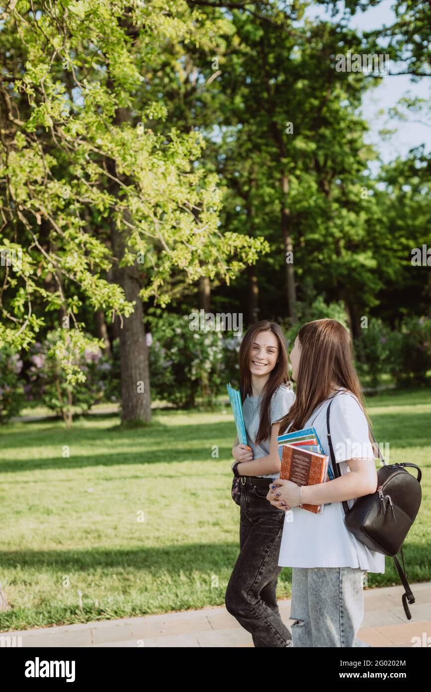 Two happy smiling student girls are walking and talking to each other ...