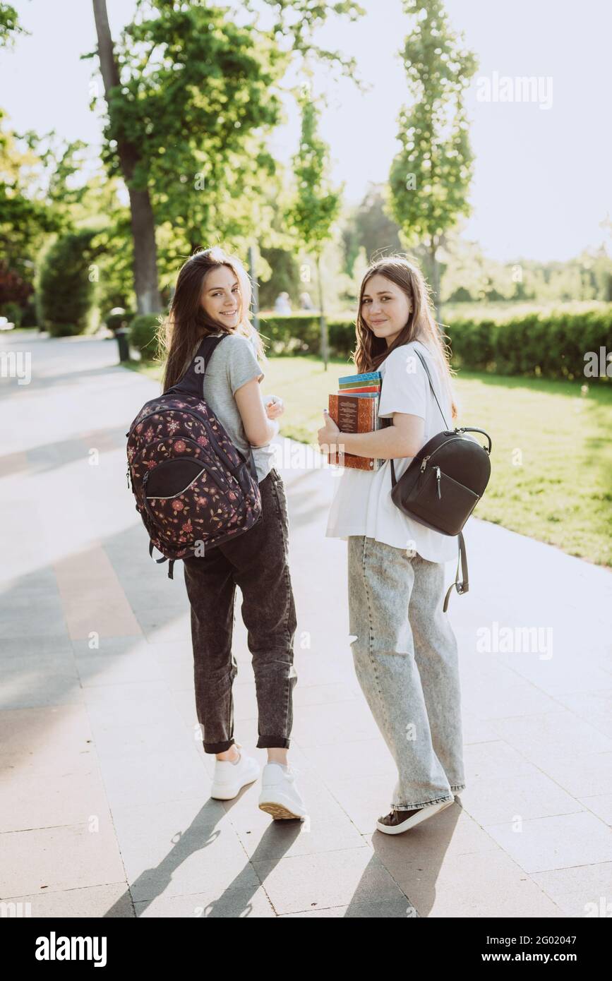 Two happy smiling student girls are walking and talking to each other ...