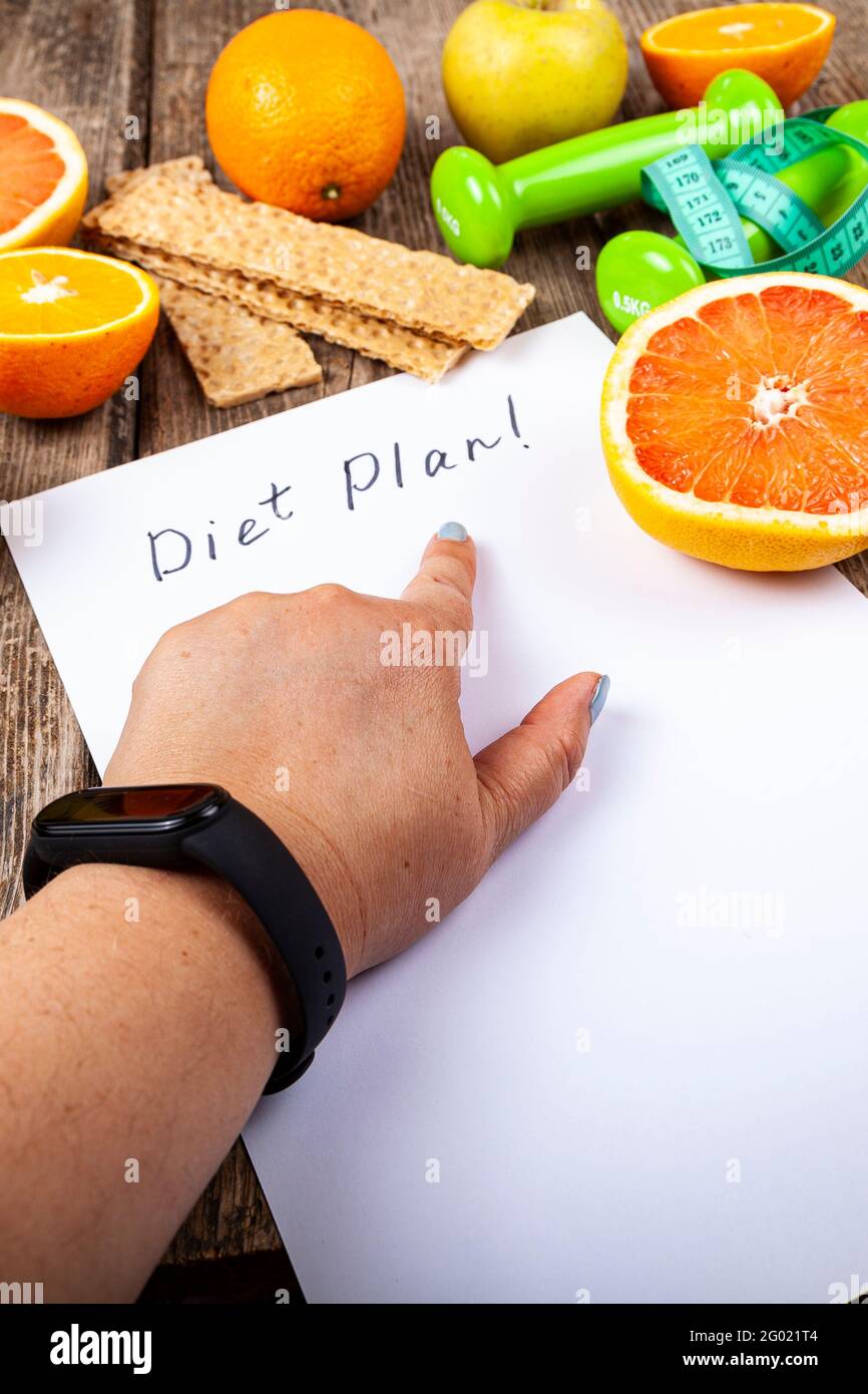 Female hand shows the diet plan. Healthy food, dumbbells and measuring ...