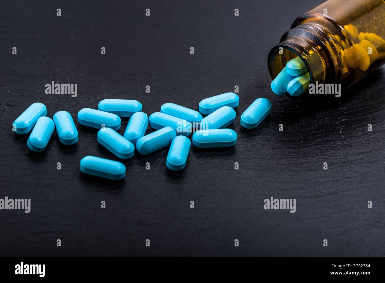 Blue pills in a bottle, medicines painkiller. Medications on a black ...