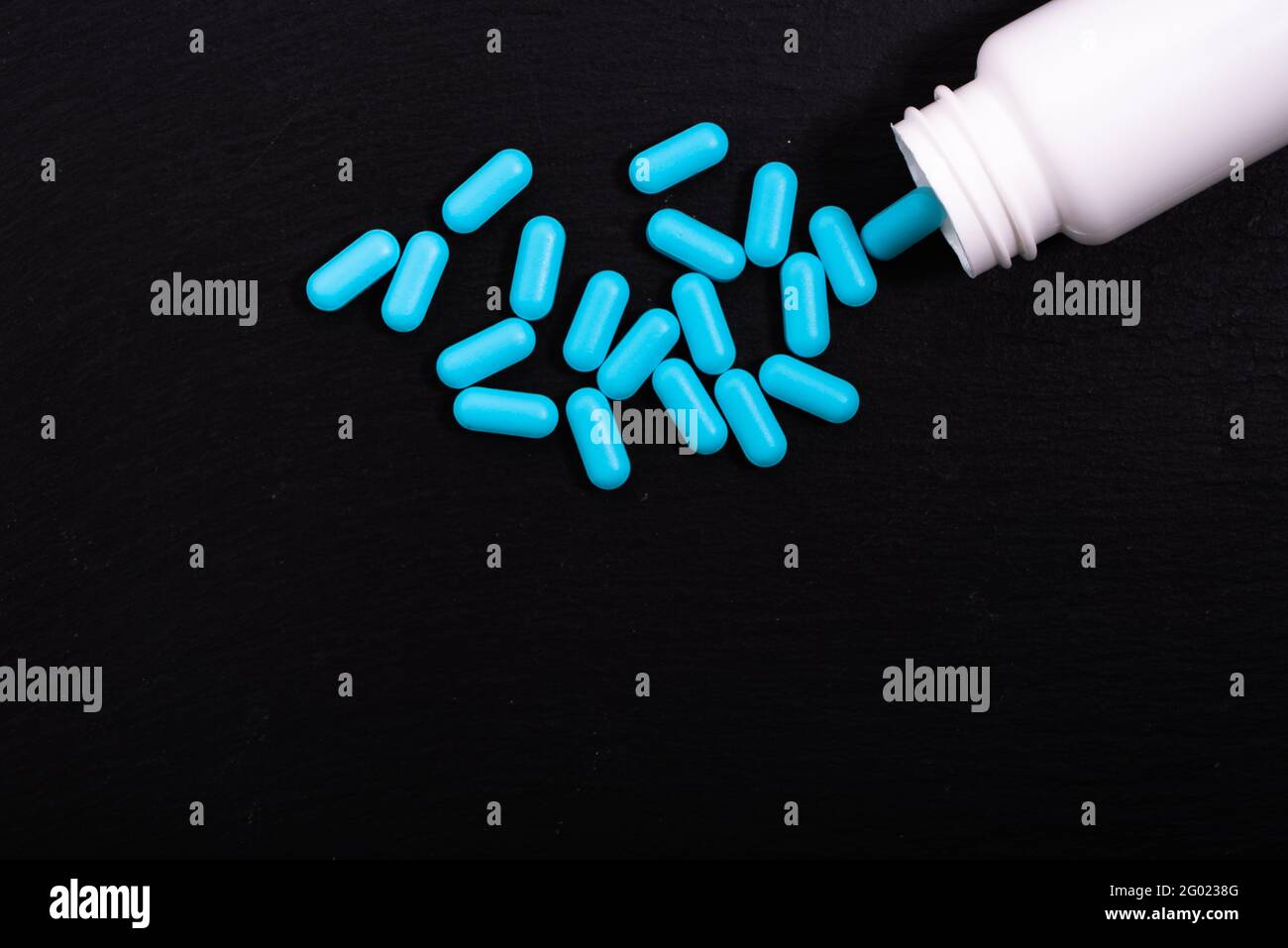Blue pills in a bottle, medicines painkiller. Medications on a black ...