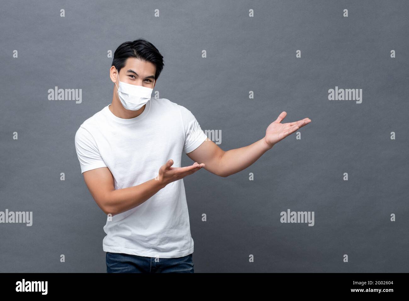 Young Asian man wearing face mask opening hands to empty space aside in ...