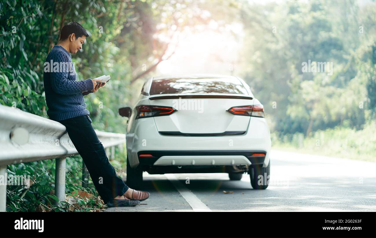 Asian traveler man standing and reading a book on the road with his car ...