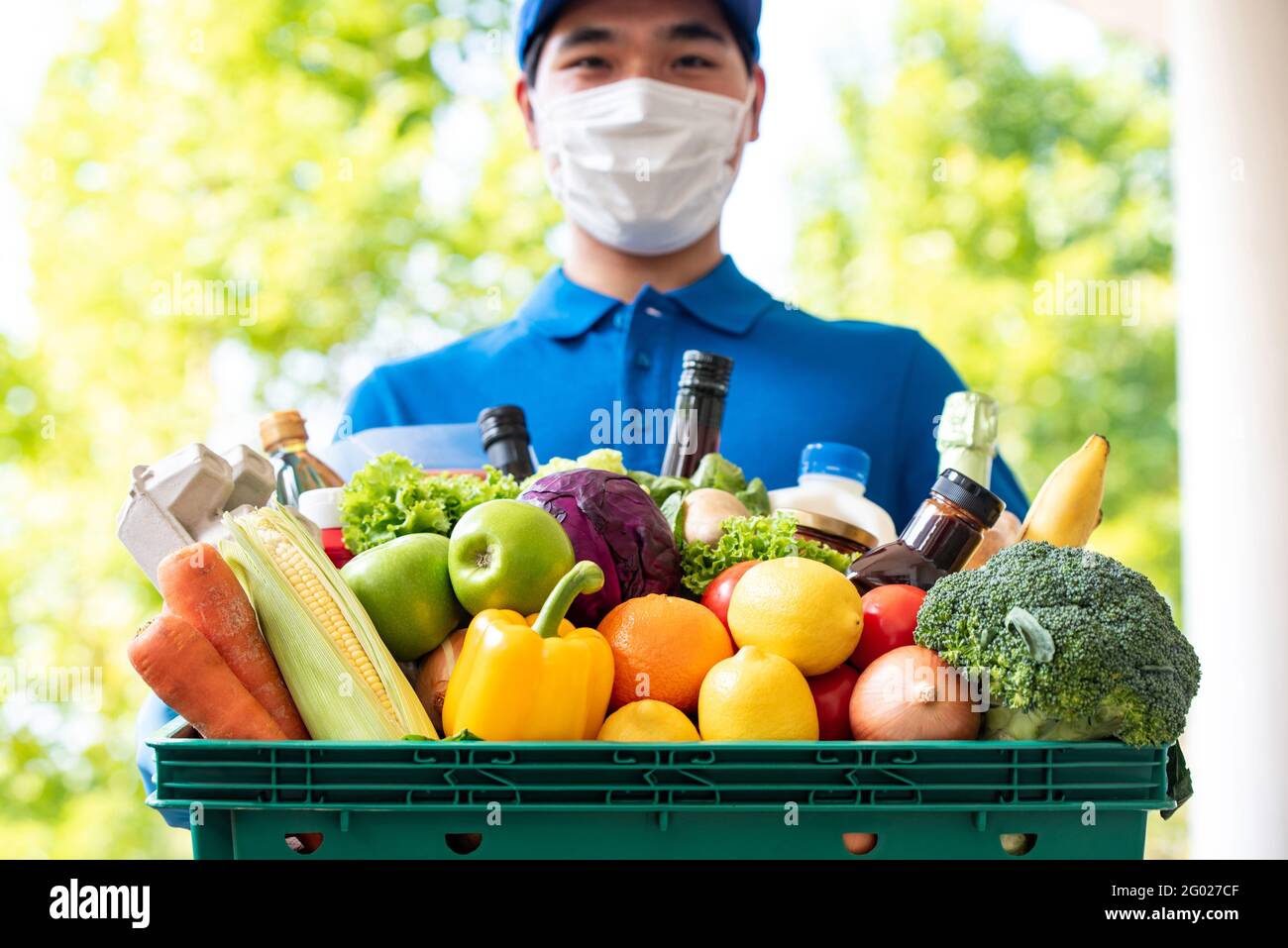 Asian deliveryman wearing face mask holding grocery basket outdoors ...