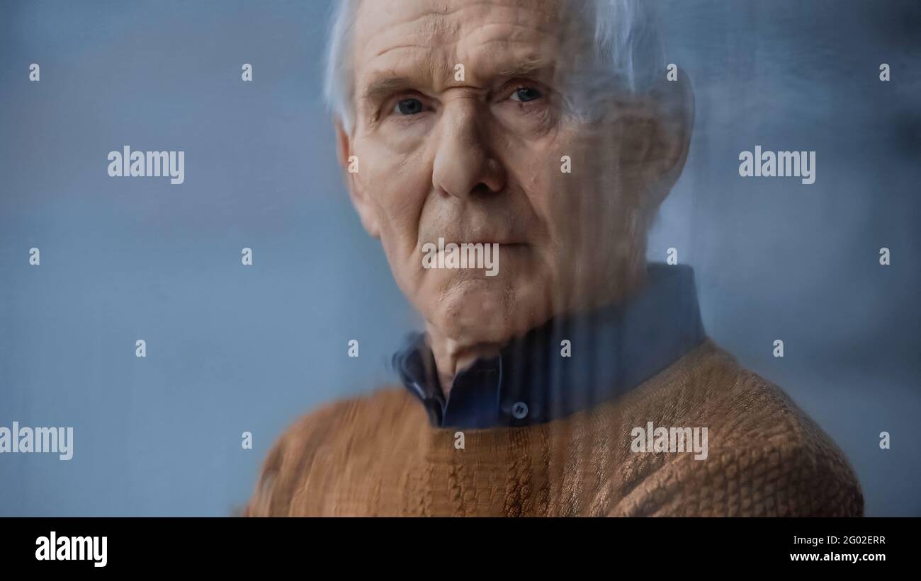 portrait of elderly man looking at camera through rainy window on grey ...