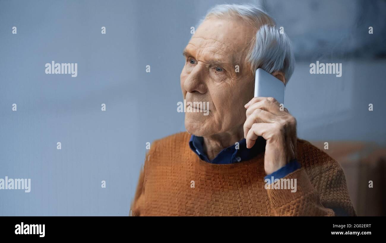 sad elderly man speaking on cellphone on grey background behind rainy ...