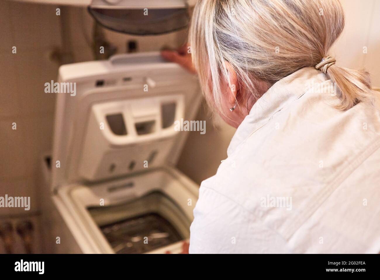 Housewife checks a top loading washing machine in the bathroom before ...
