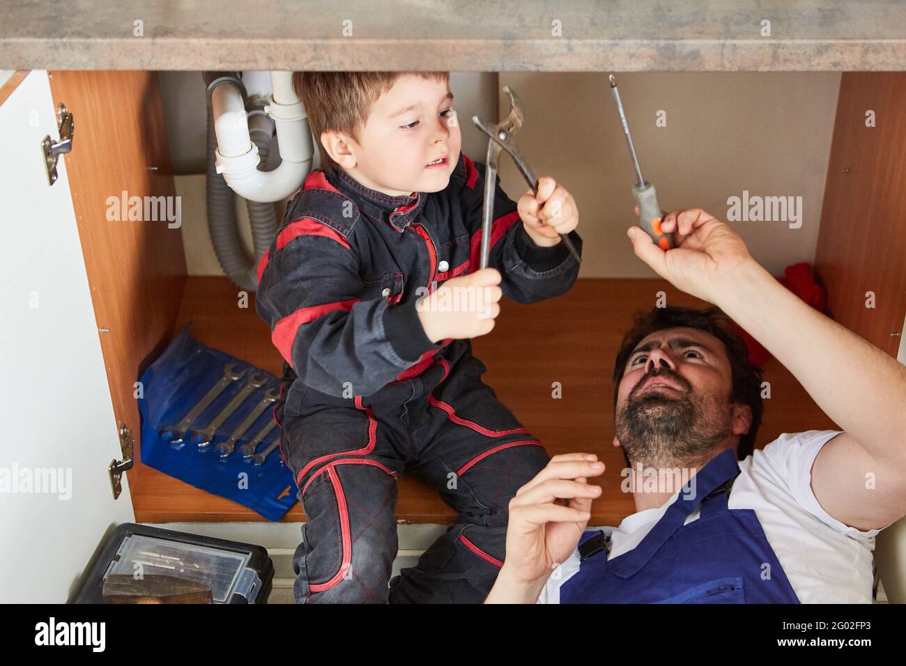Child helping his father repair a sink in the kitchen as a handyman ...