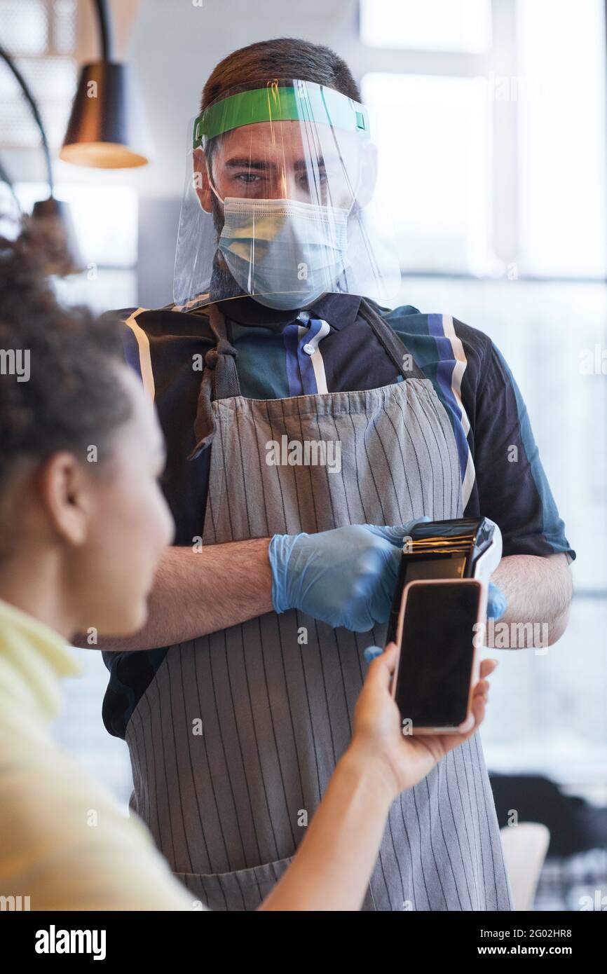 Vertical portrait of waiter wearing face shield and gloves while ...