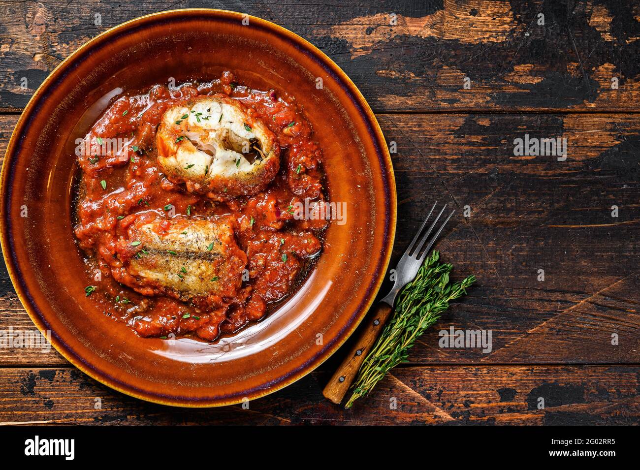 Roast hake white fish fillet with tomato sauce in a plate. Dark ...