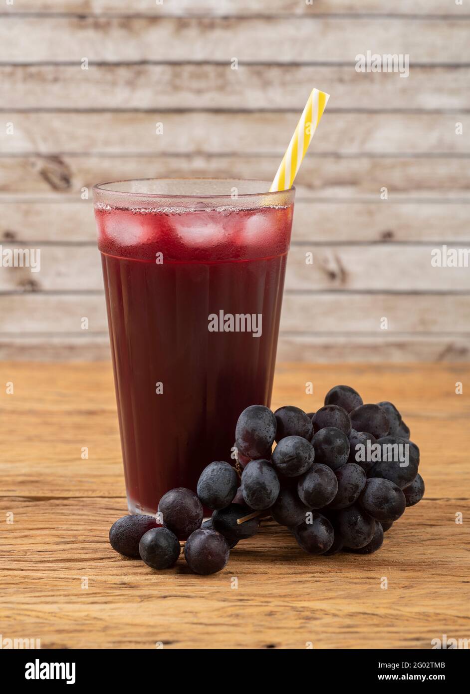 Red grape juice in a glass with ice and fruits over wooden table Stock ...