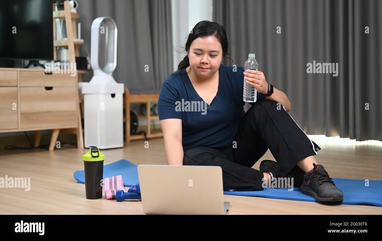 Happy obese young woman taking a break and drinking water during ...
