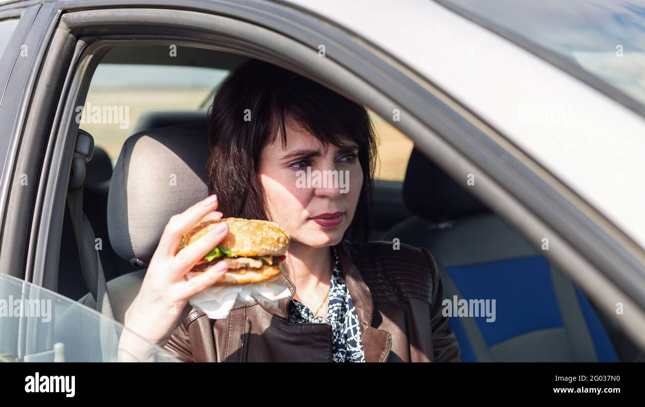 A woman with fast food at the wheel concept of poor nutrition in modern ...