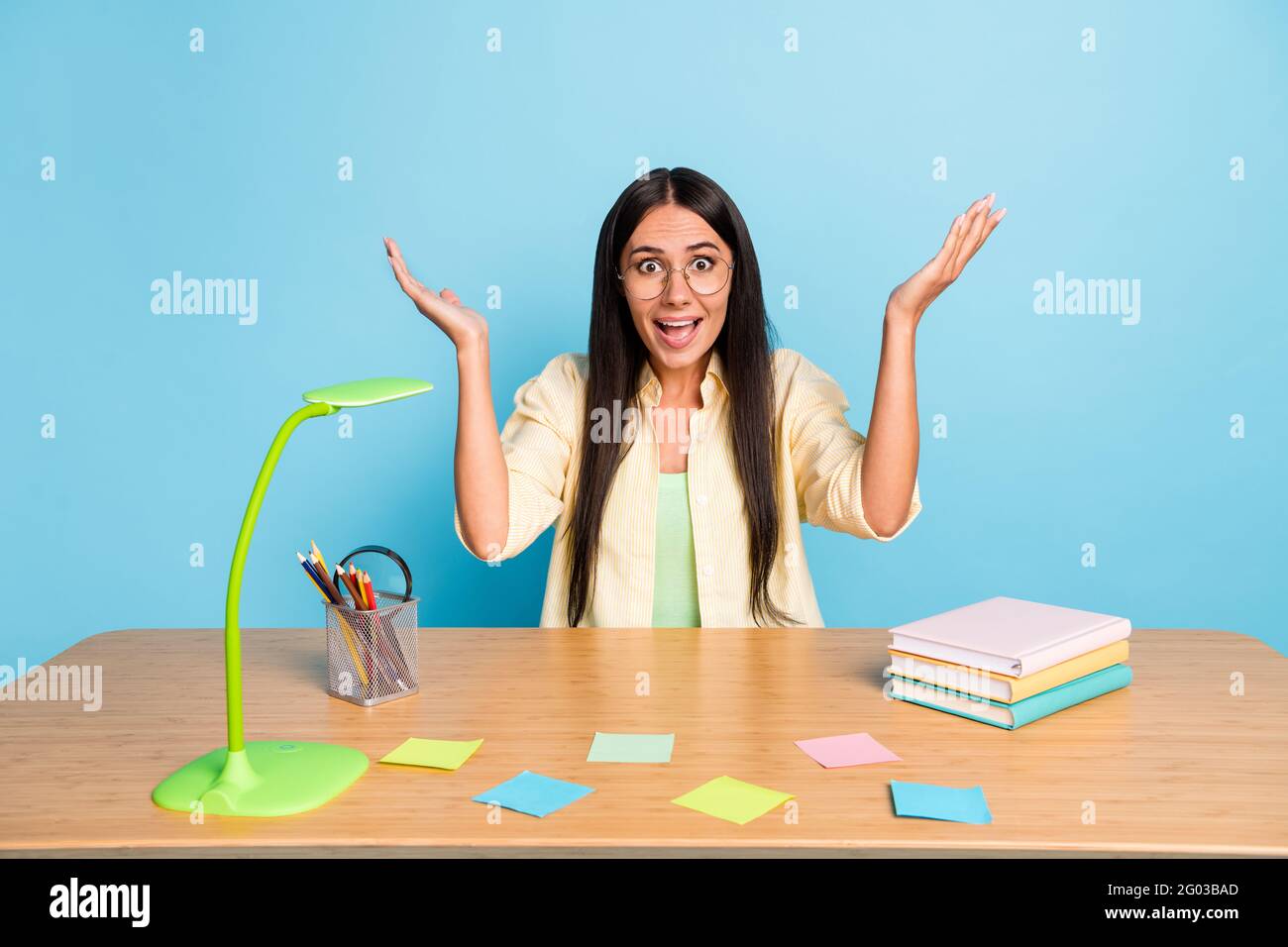 Photo of shocked amazed young woman sit table raise hands unexpected ...