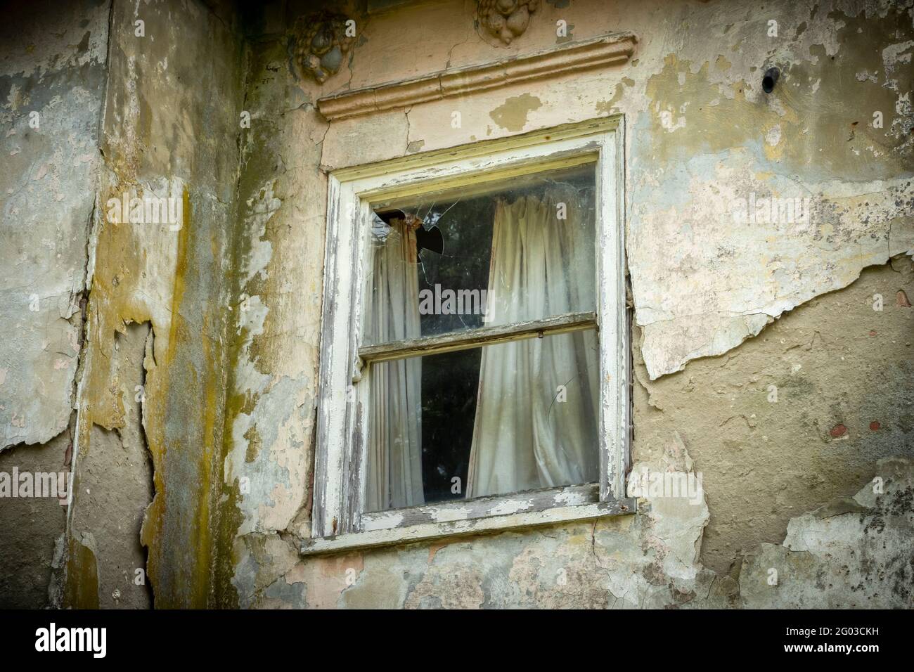 A damaged sash window with curtain remnants in an abandonedpart ruined ...