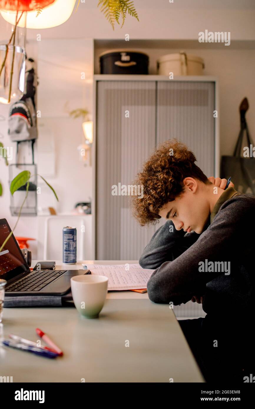 Tired boy reading book while studying at home Stock Photo - Alamy