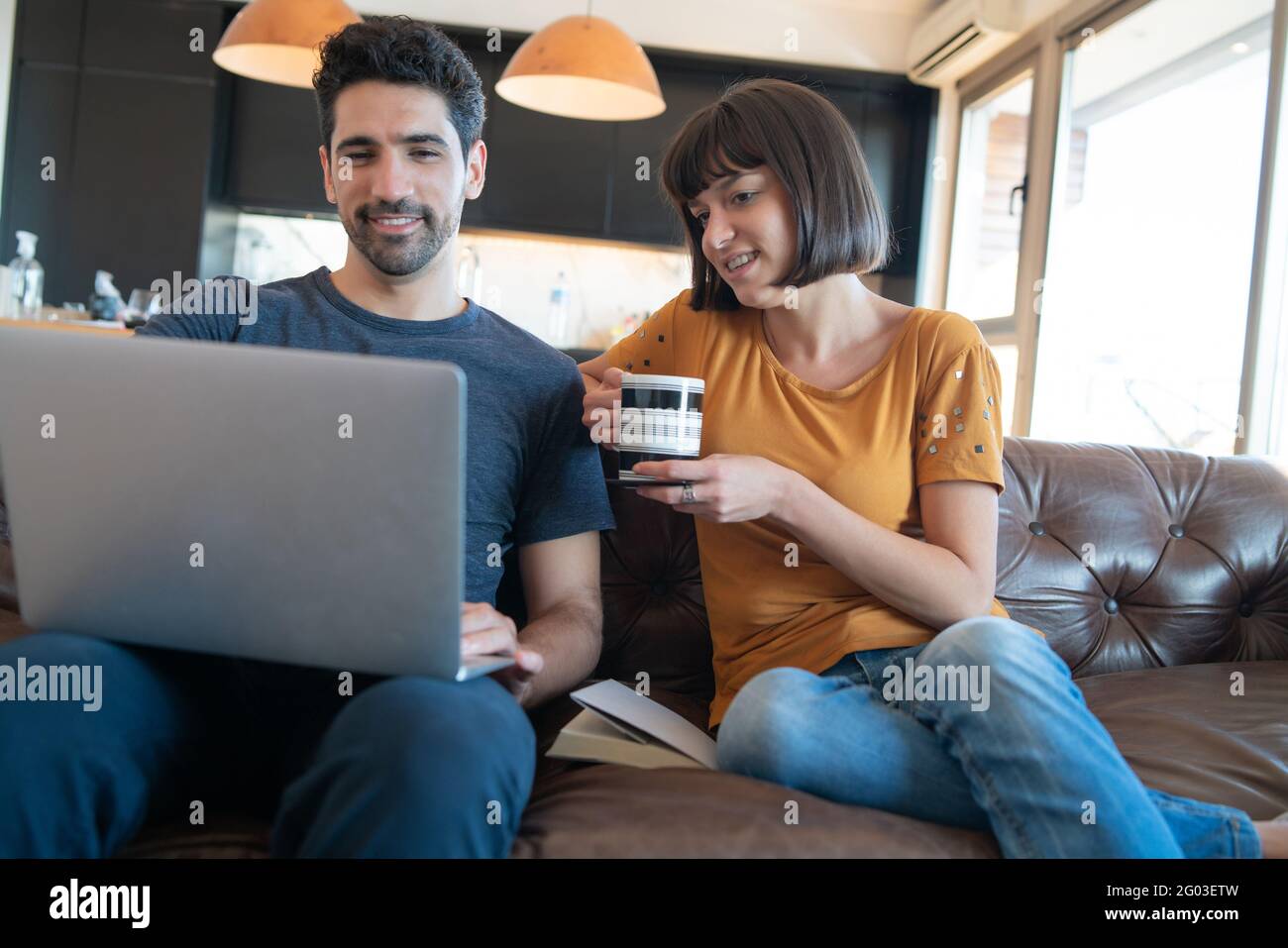 Couple using laptop while sitting on couch at home Stock Photo - Alamy