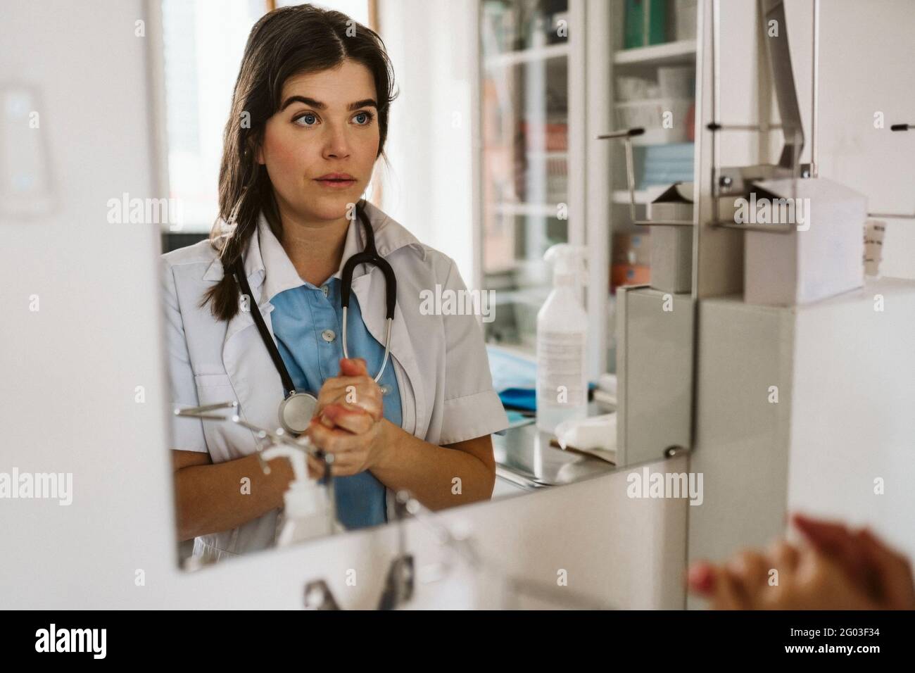 Female medical expert looking in mirror while washing hands Stock Photo ...