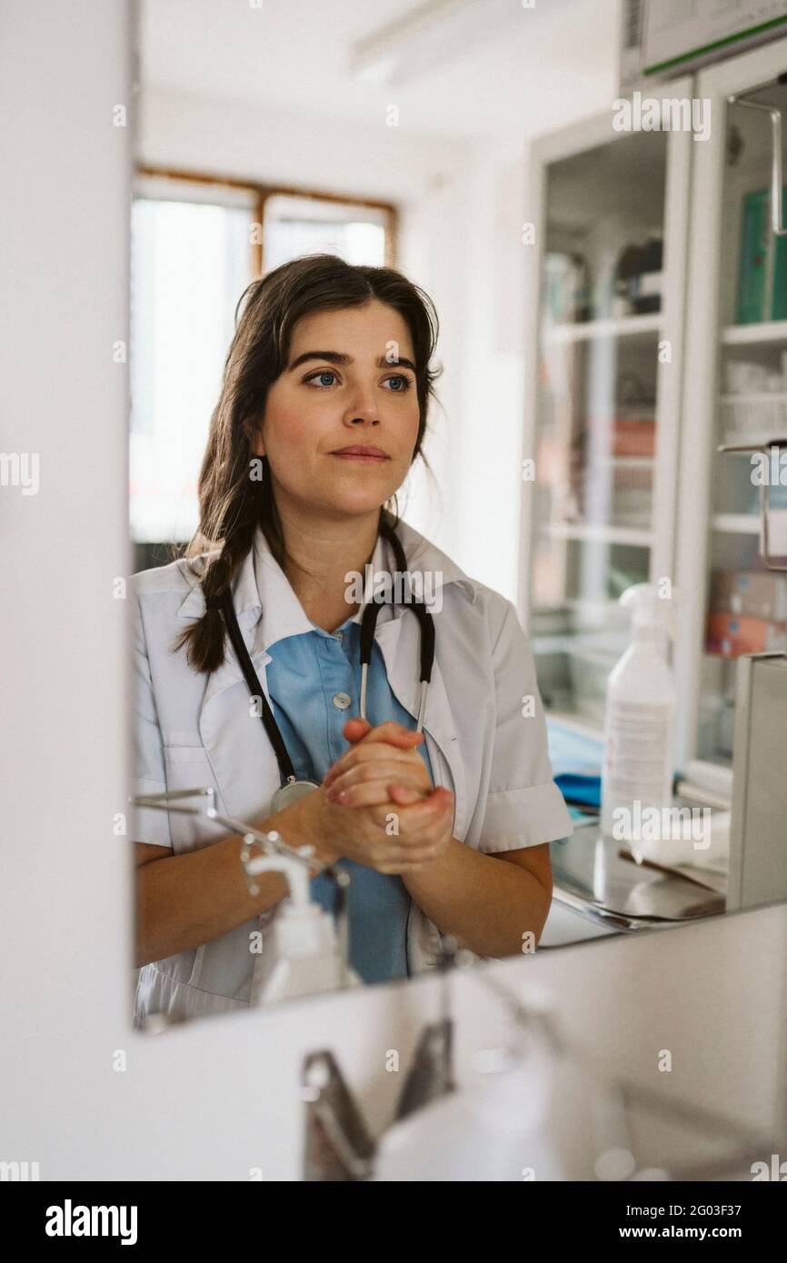 Female healthcare expert looking in mirror while washing hands in ...