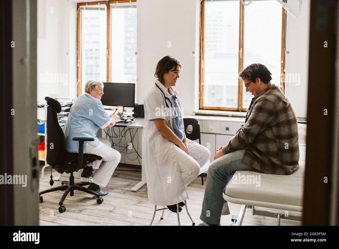 Smiling female healthcare worker talking with young male patient while ...