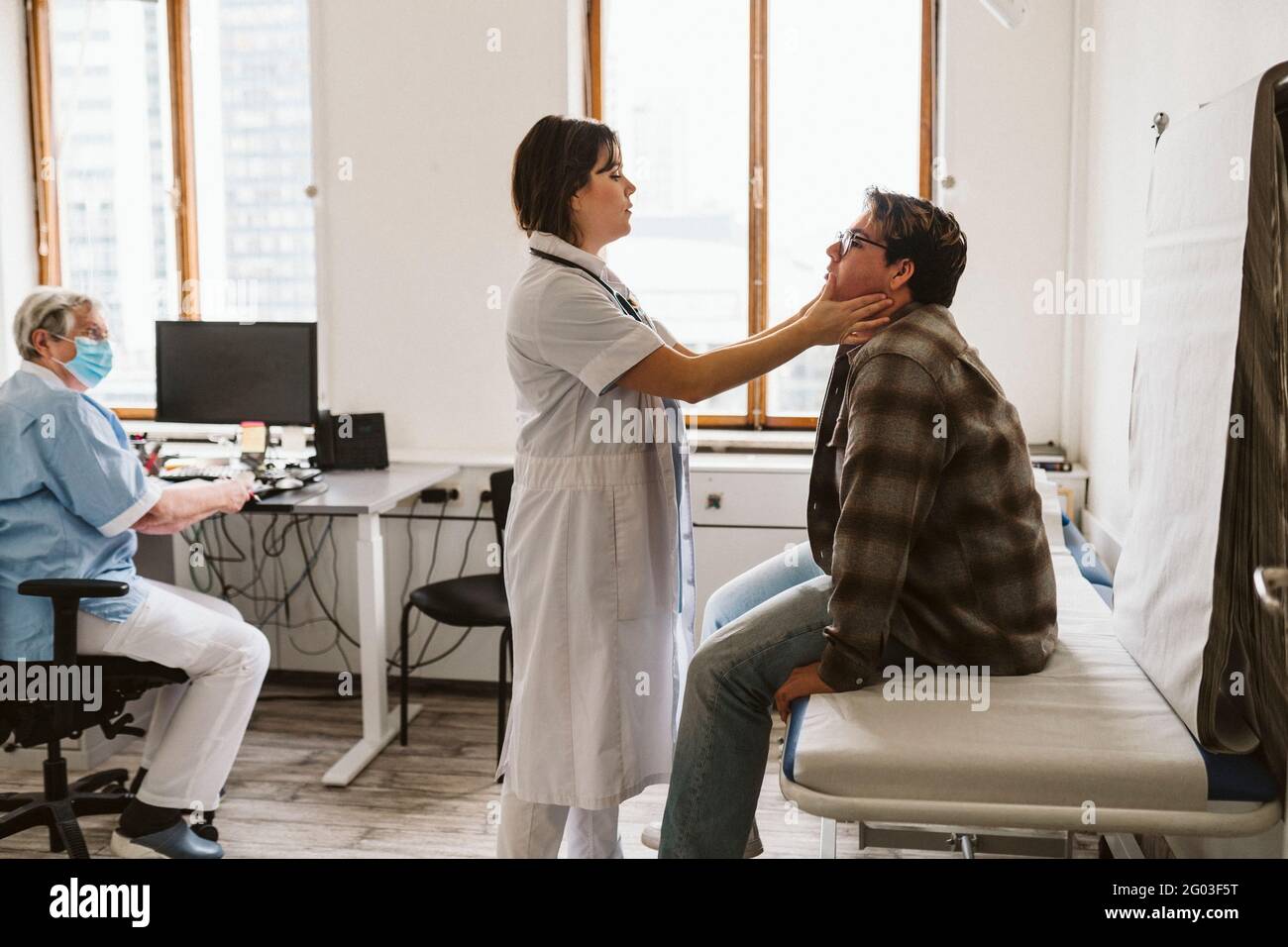 Senior female nurse looking at doctor checking pulse of male patient in ...