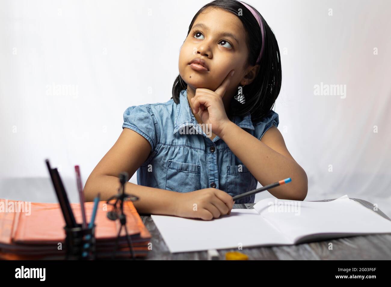 A pretty Indian girl child thinking and looking upward while studying ...